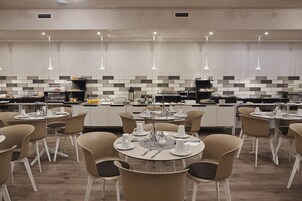 Uma sala de jantar moderna com mesas e cadeiras redondas, painel de azulejos e iluminação pendente.