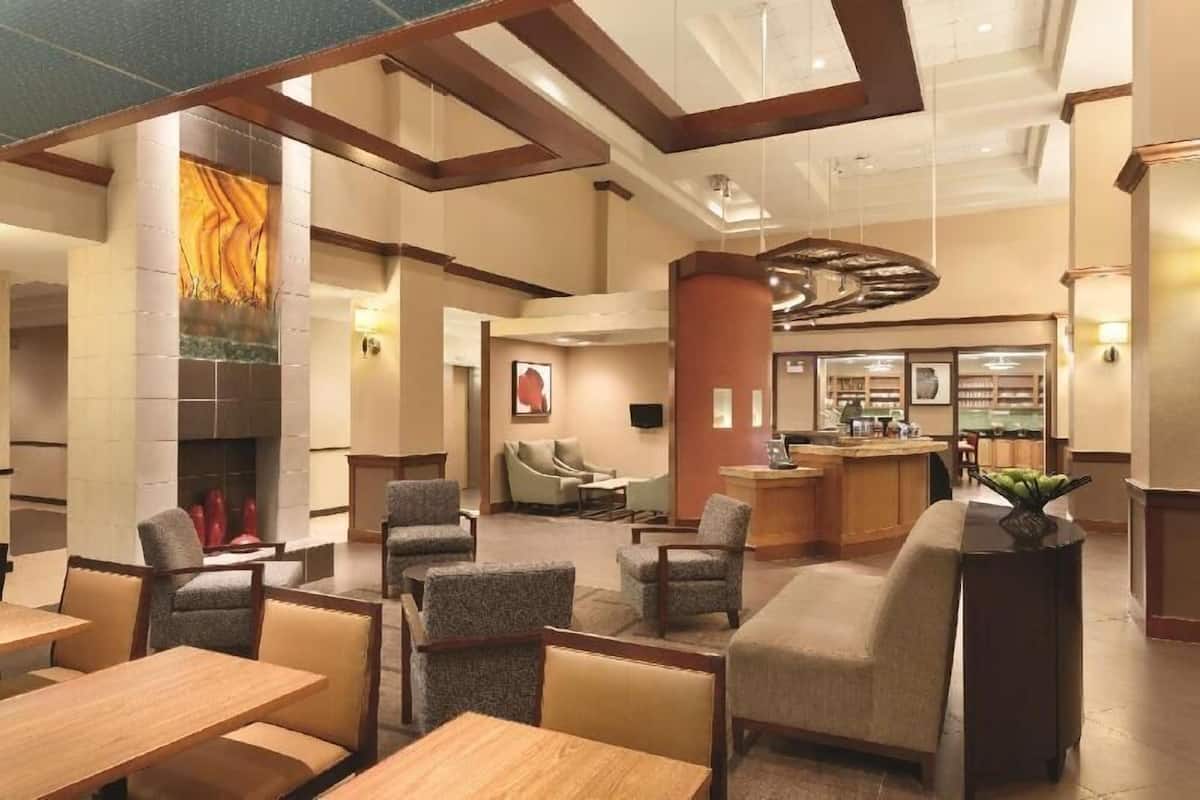 Um hall de hotel com áreas de estar, lareira, bar e uma grande obra de arte na parede.