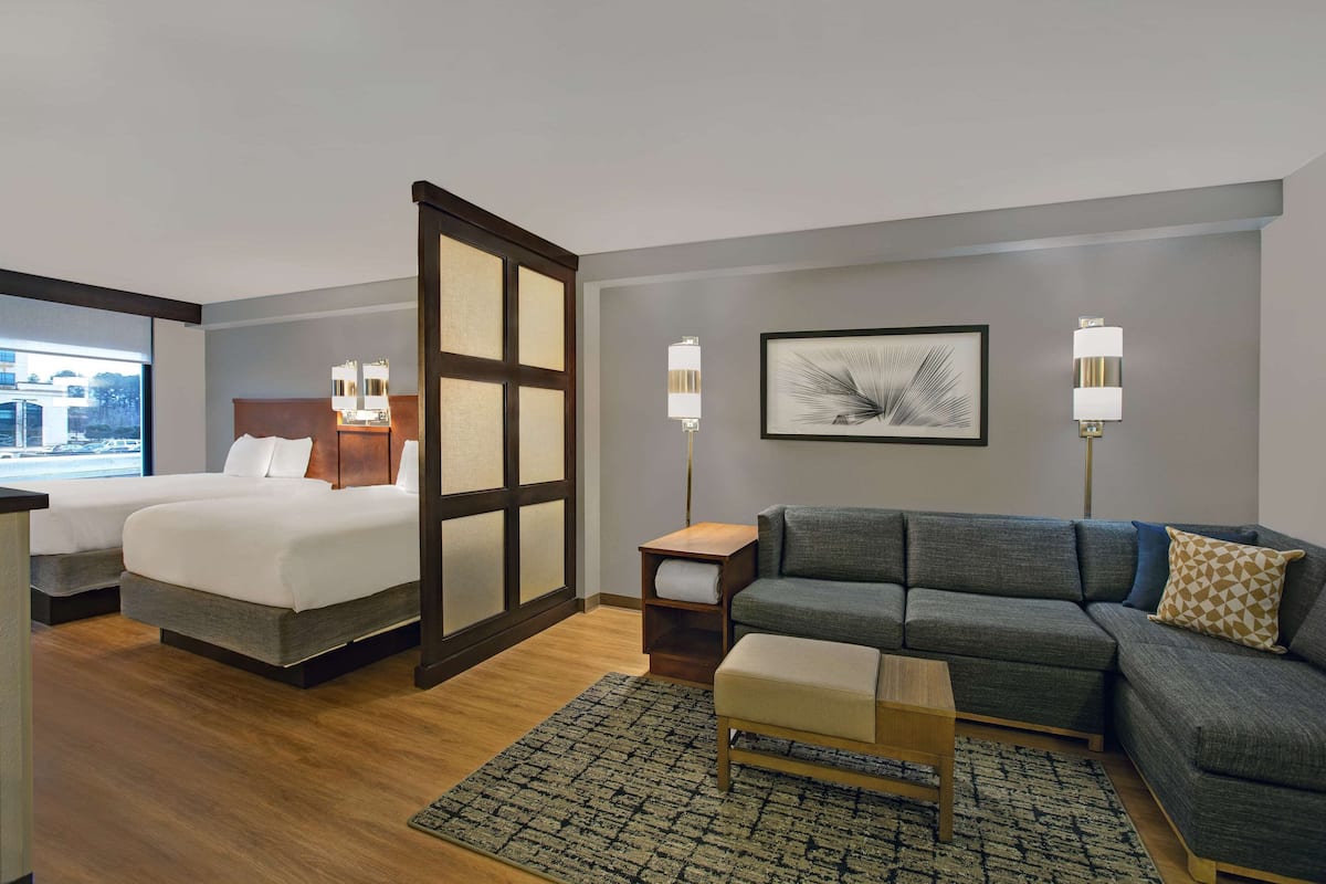 Quarto de hotel com duas camas, um sofá, uma mesinha e um abajur.