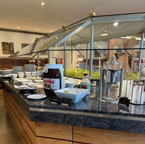 Uma área de buffet com divisória de vidro, um pote grande de Nutella e diversos alimentos.