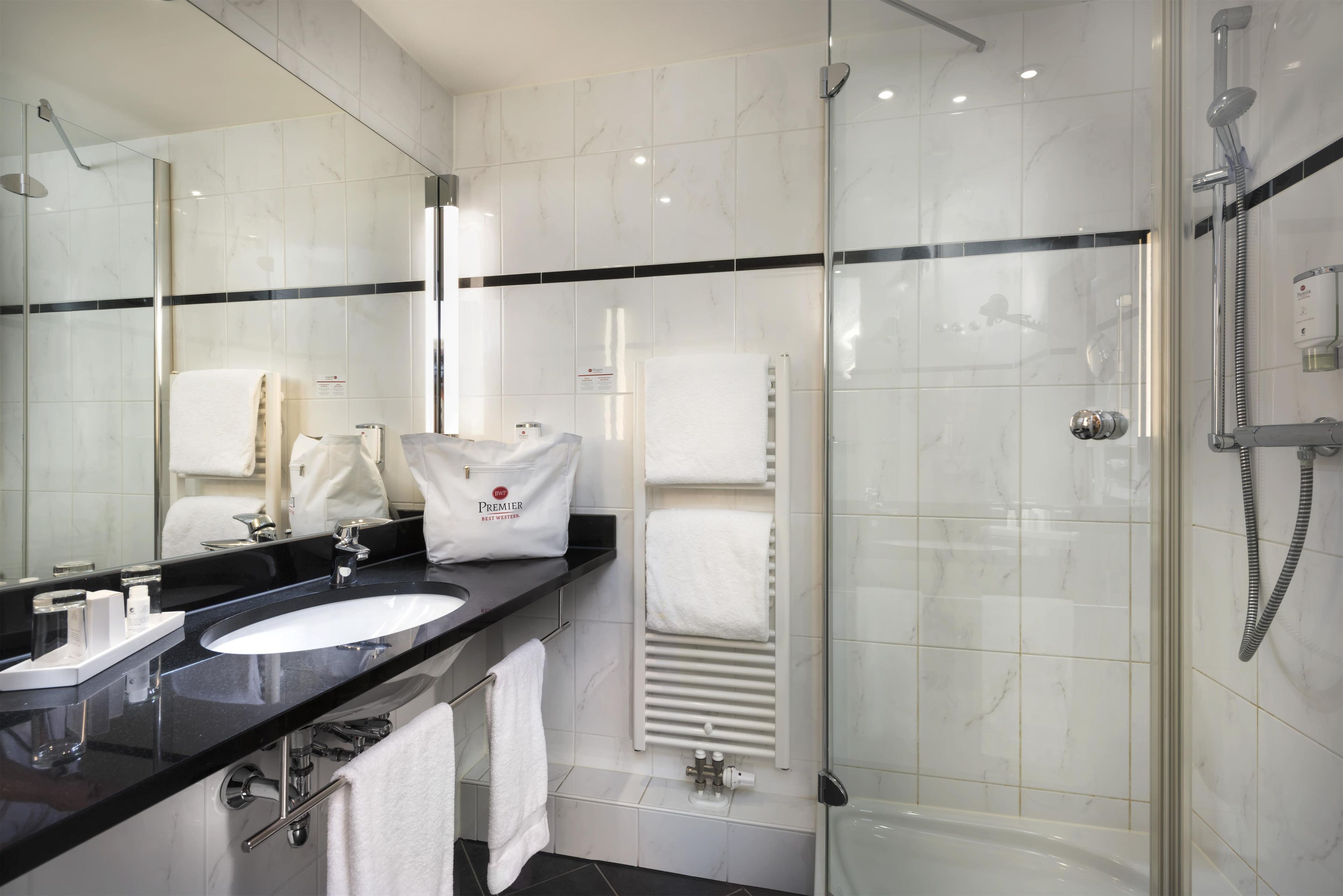 Um banheiro moderno com bancada preta, azulejos de mármore branco e box de vidro, além de um espelho.