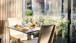 Uma mesa de jantar com itens de café da manhã e vista para a cidade através de grandes janelas.