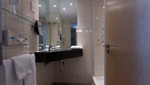 Um banheiro moderno com pia preta, azulejos brancos, box de vidro e porta de madeira.