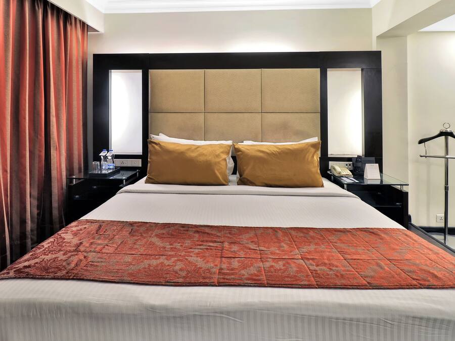 Quarto de hotel com uma cama grande, duas almofadas, uma mesa de cabeceira, um abajur e um guarda-roupa.