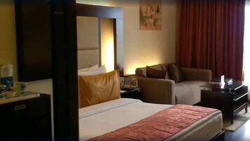 Quarto de hotel com cama, sofá, escrivaninha com luminária e piano.