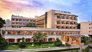 Um hotel com vários andares, varandas, um jardim bem cuidado e uma placa com a inscrição "Bella Plaza".