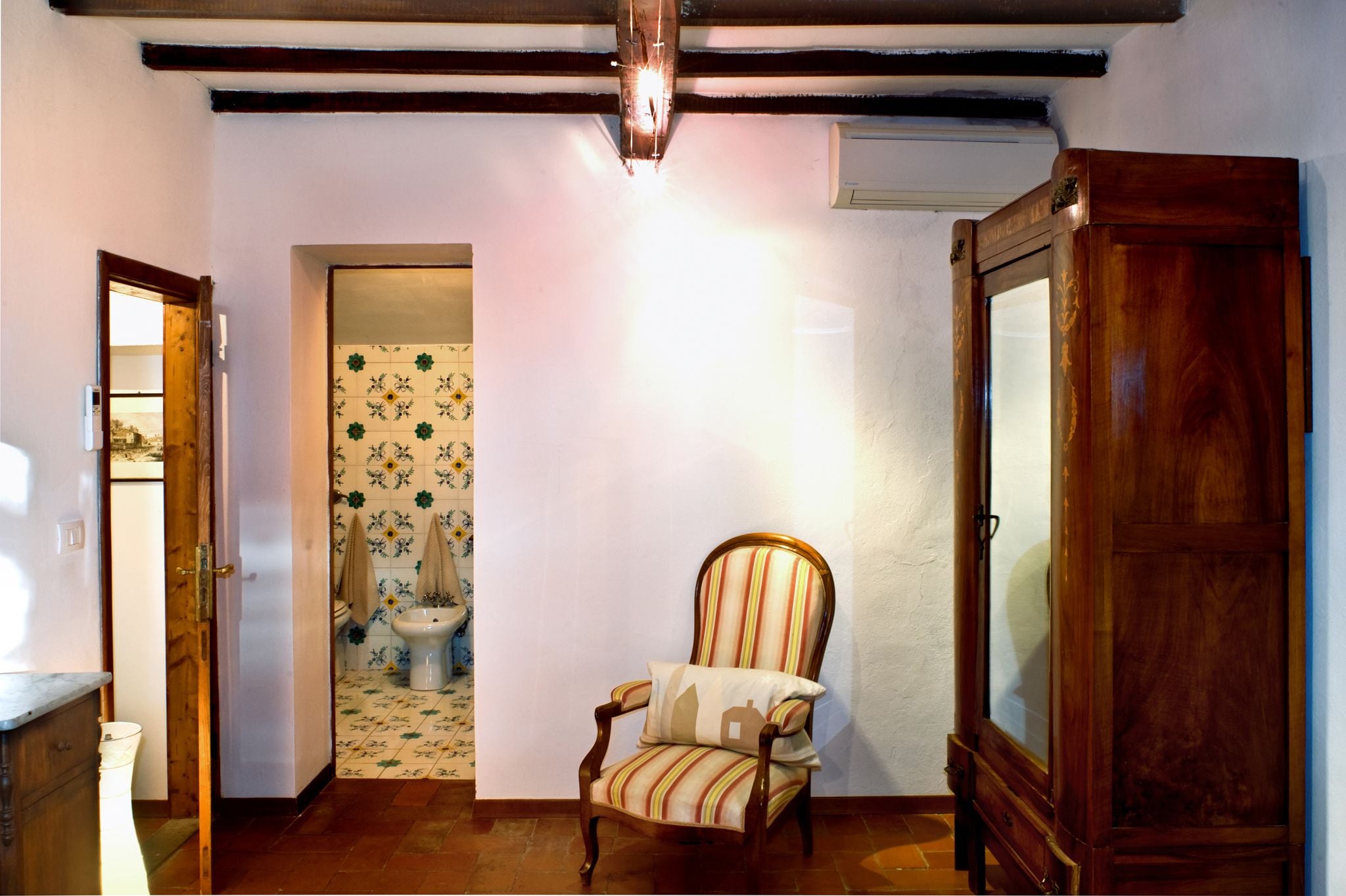 Um quarto com uma cadeira e um armário de madeira, e piso de azulejos.