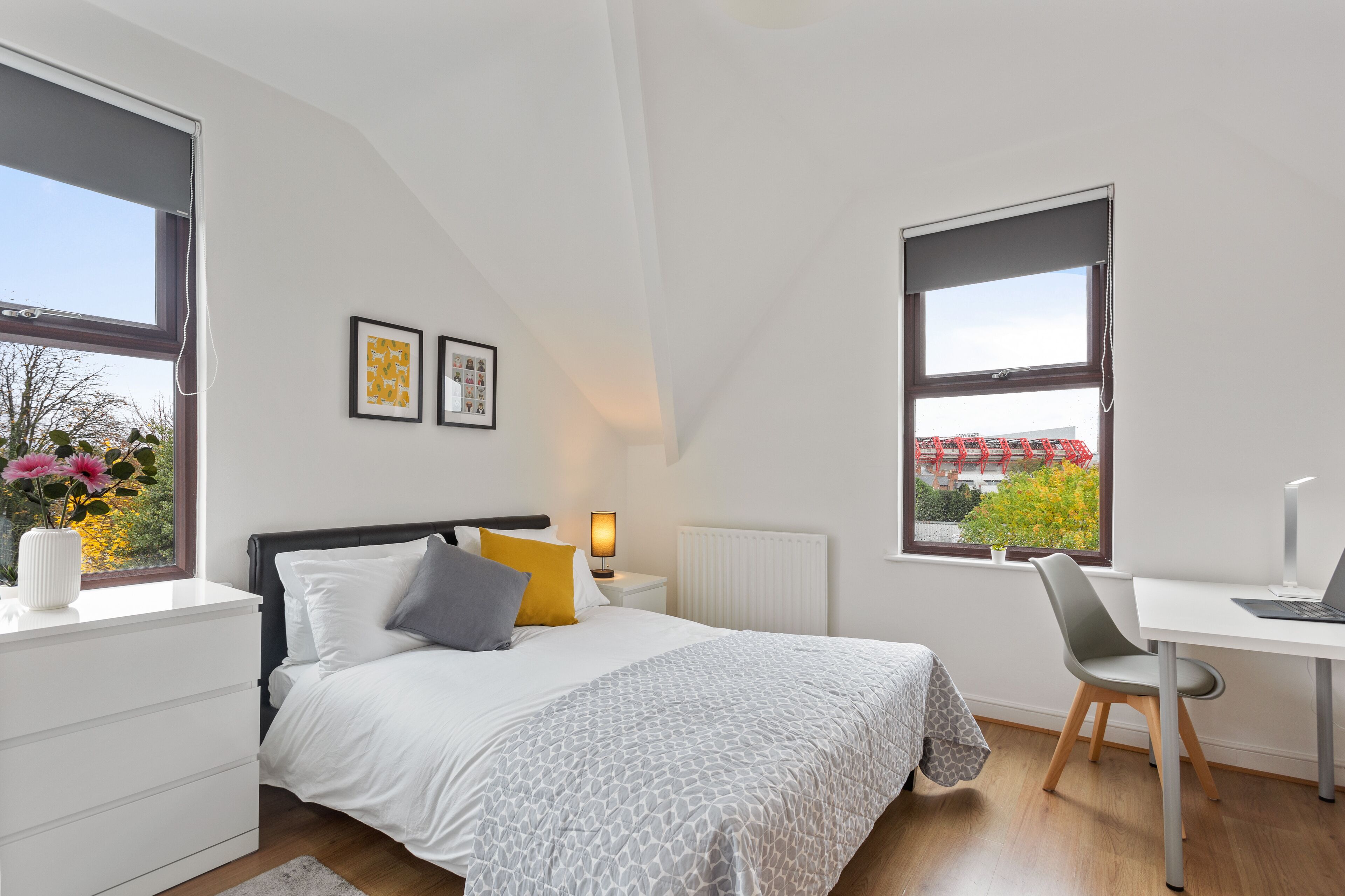 Quarto moderno com cama, mesa de cabeceira, luminária e escrivaninha com cadeira.