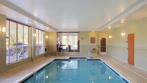 Uma piscina interior com paredes de vidro transparente, chão revestido de azulejos e uma porta que dá para o exterior.