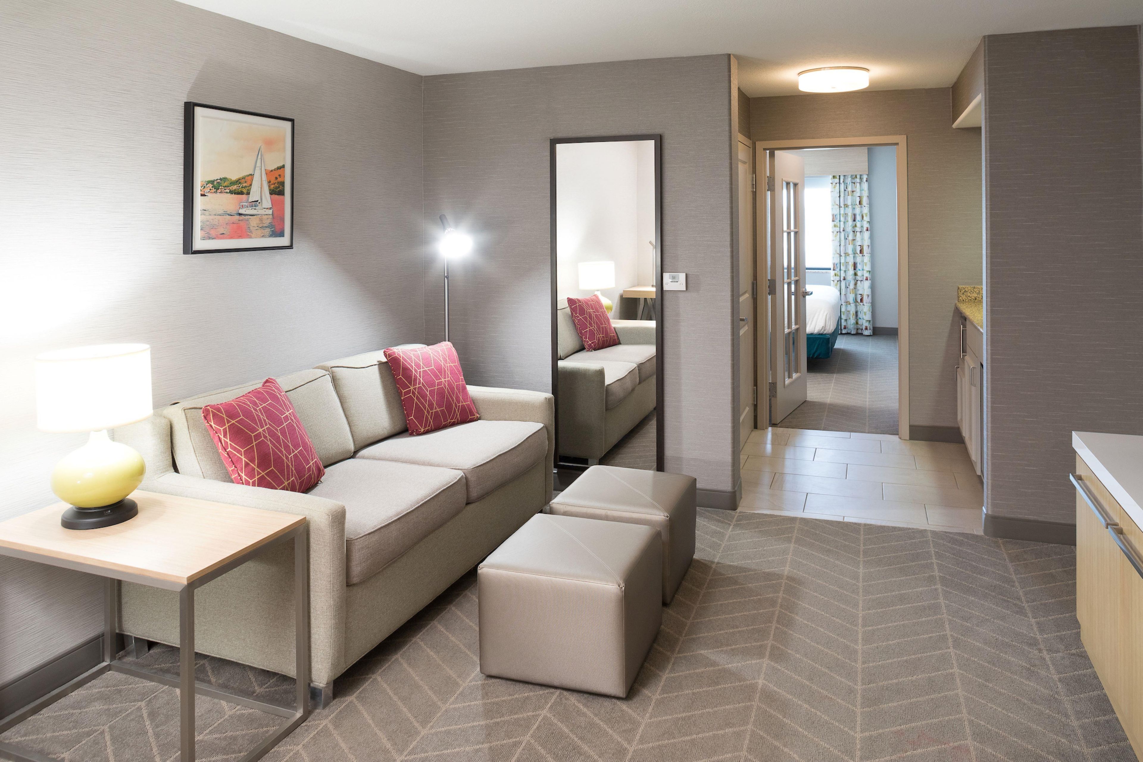 Quarto de hotel moderno com sofá, banquinho e escrivaninha com abajur.
