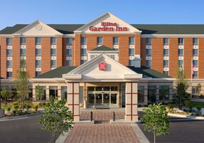 Um Hilton Garden Inn com fachada de tijolos, entrada ampla e céu claro.