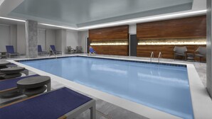Piscina interior com espreguiçadeiras, sala de trocas e parede de madeira com iluminação embutida.