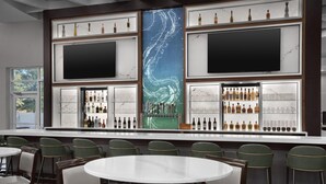Zona de bar com várias opções de assento, uma televisão grande e prateleiras com garrafas.