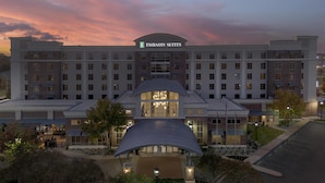 Um hotel grande e moderno, com um letreiro chamativo 'Embassy Suites', entrada coberta e área de estacionamento.