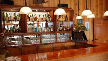 Uma área de bar com painéis de madeira, diversas garrafas de bebidas, copos e uma televisão.