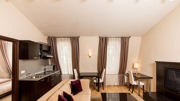 Quarto de hotel moderno com cozinha compacta, sofá, mesa de jantar e TV.