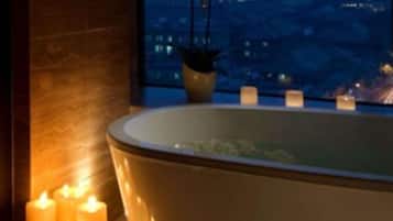 Um banheiro moderno com uma banheira independente, velas e vista para o horizonte ao anoitecer.