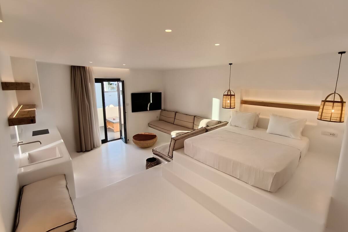 Quarto de hotel moderno com uma cama grande, um sofá, uma TV, uma escrivaninha e um banheiro.