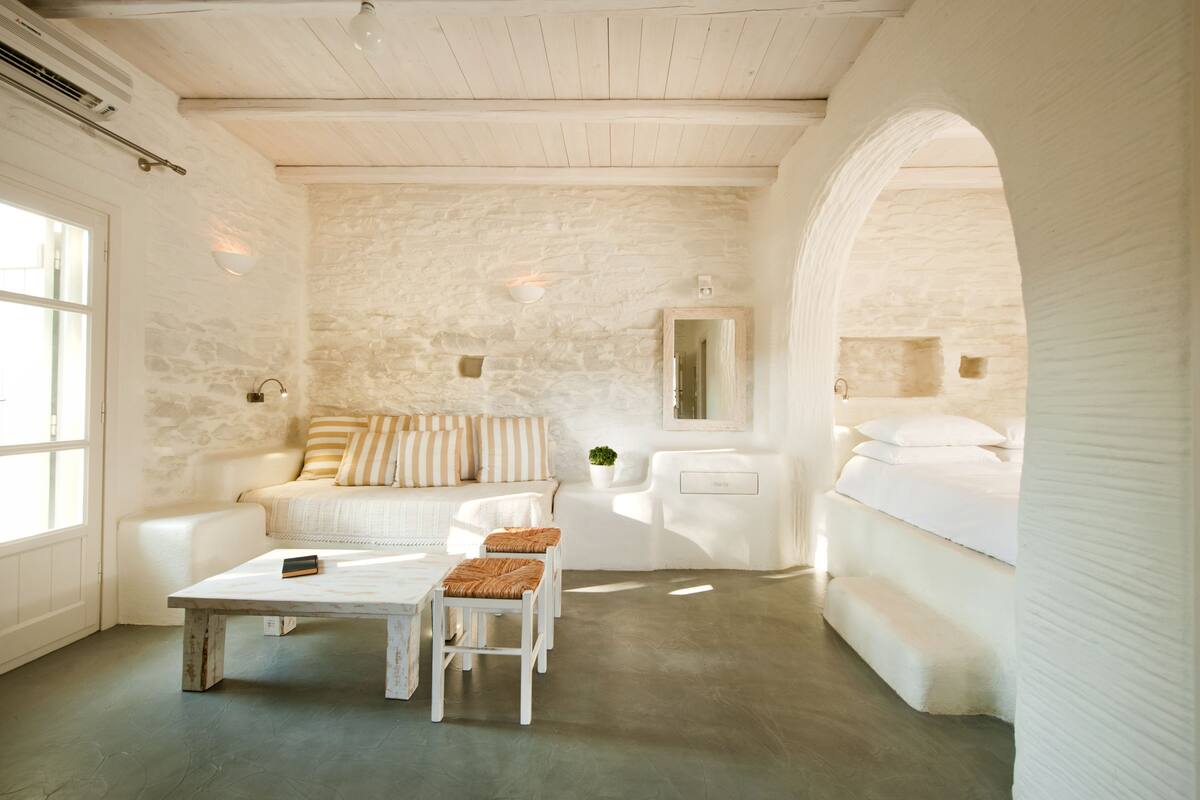 Quarto minimalista com parede de pedra, sofá branco, mesa pequena e cama.