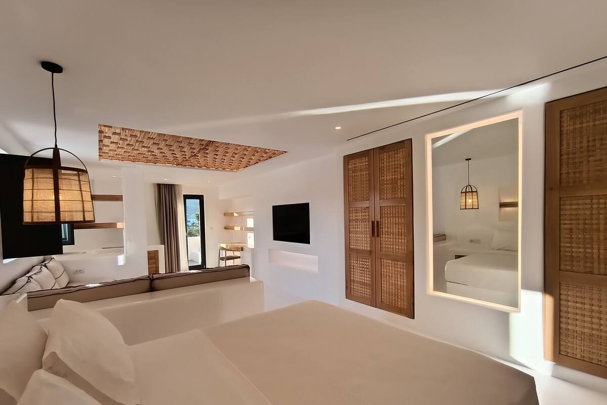 Quarto de hotel moderno com cama grande, televisão, espelho e varanda com vista.
