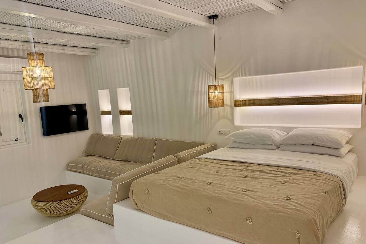 Quarto moderno com cama grande, sofá, televisão e luminária pendente única.