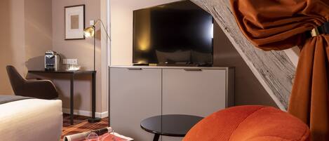 Quarto de hotel com cama, secretária com cafeteira, televisão e uma pequena mesa com uma revista.