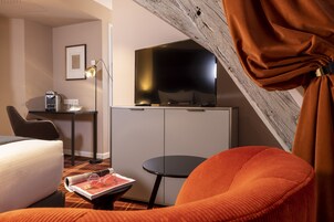 Quarto de hotel com cama, secretária com cafeteira, televisão e uma pequena mesa com uma revista.