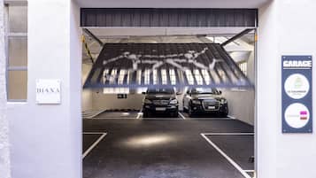 Uma garagem com dois carros, uma placa indicando 'Garage' e uma placa para 'Diana Hotels Collection'.