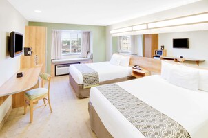Quarto de hotel com duas camas, uma escrivaninha, uma cadeira, uma televisão e uma janela com cortinas.