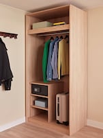 Guarda-roupa de madeira com roupas penduradas, uma pequena estante com livros e uma mala.