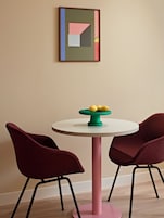 Quarto com uma mesa redonda, duas cadeiras, uma obra de arte na parede e uma fruteira sobre a mesa.