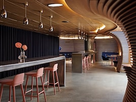 Uma área de bar moderna com teto curvo, banquetas e iluminação pendente.
