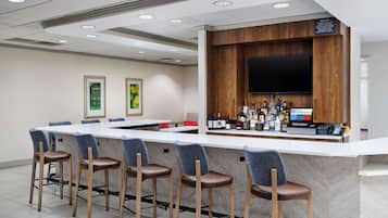 Uma área de bar com um balcão comprido, banquetas e uma TV montada na parede.