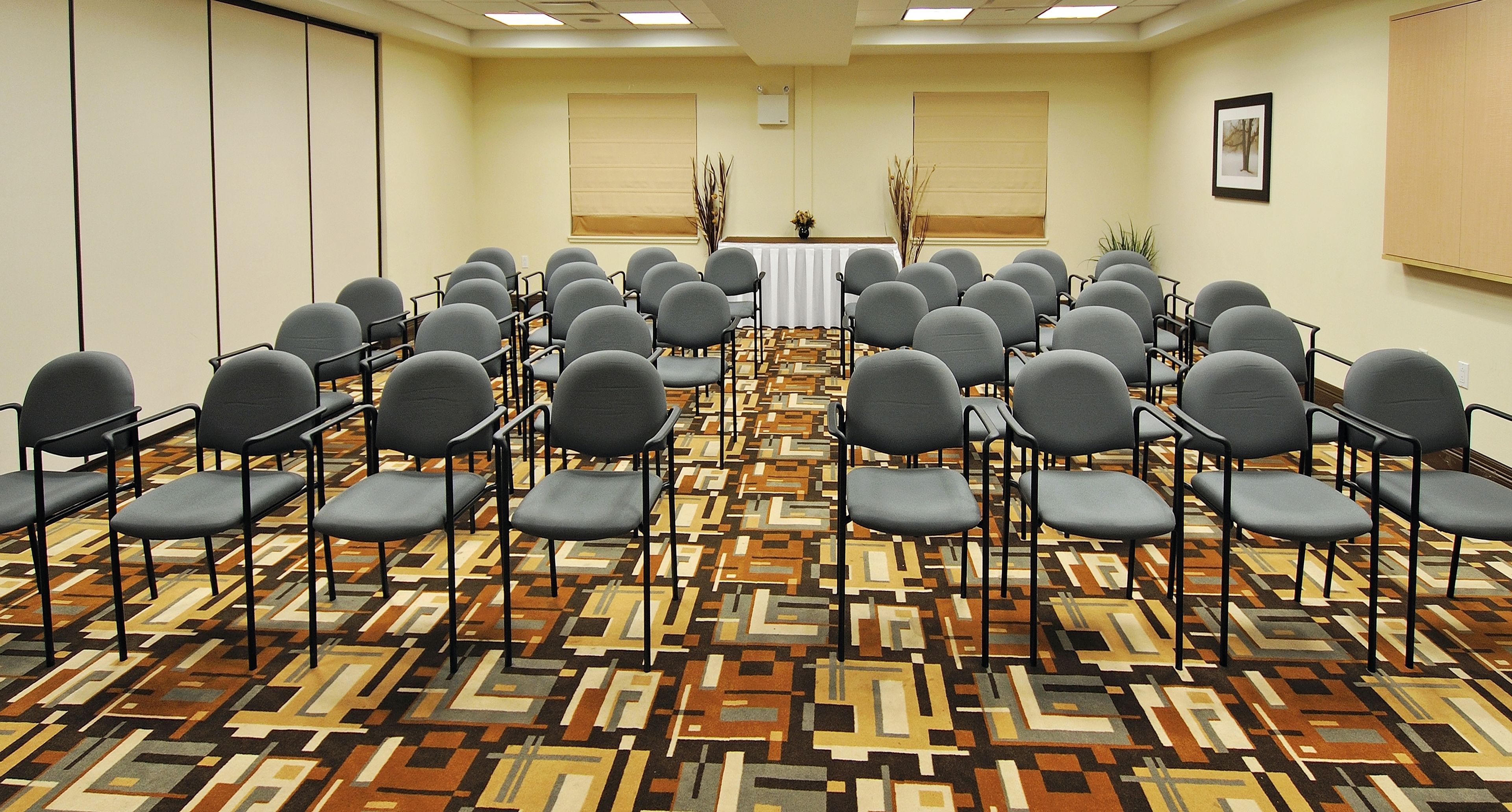 Uma sala de conferências com fileiras de cadeiras, um tapete estampado e uma mesa com toalha branca.