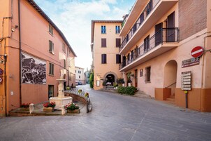 Rua estreita com edifícios em ambos os lados, uma fonte ao centro e um sinal de proibido estacionar à direita.