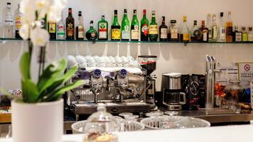 Uma área de bar com uma máquina de café, diversas garrafas de bebidas alcoólicas nas prateleiras e um vaso de planta.