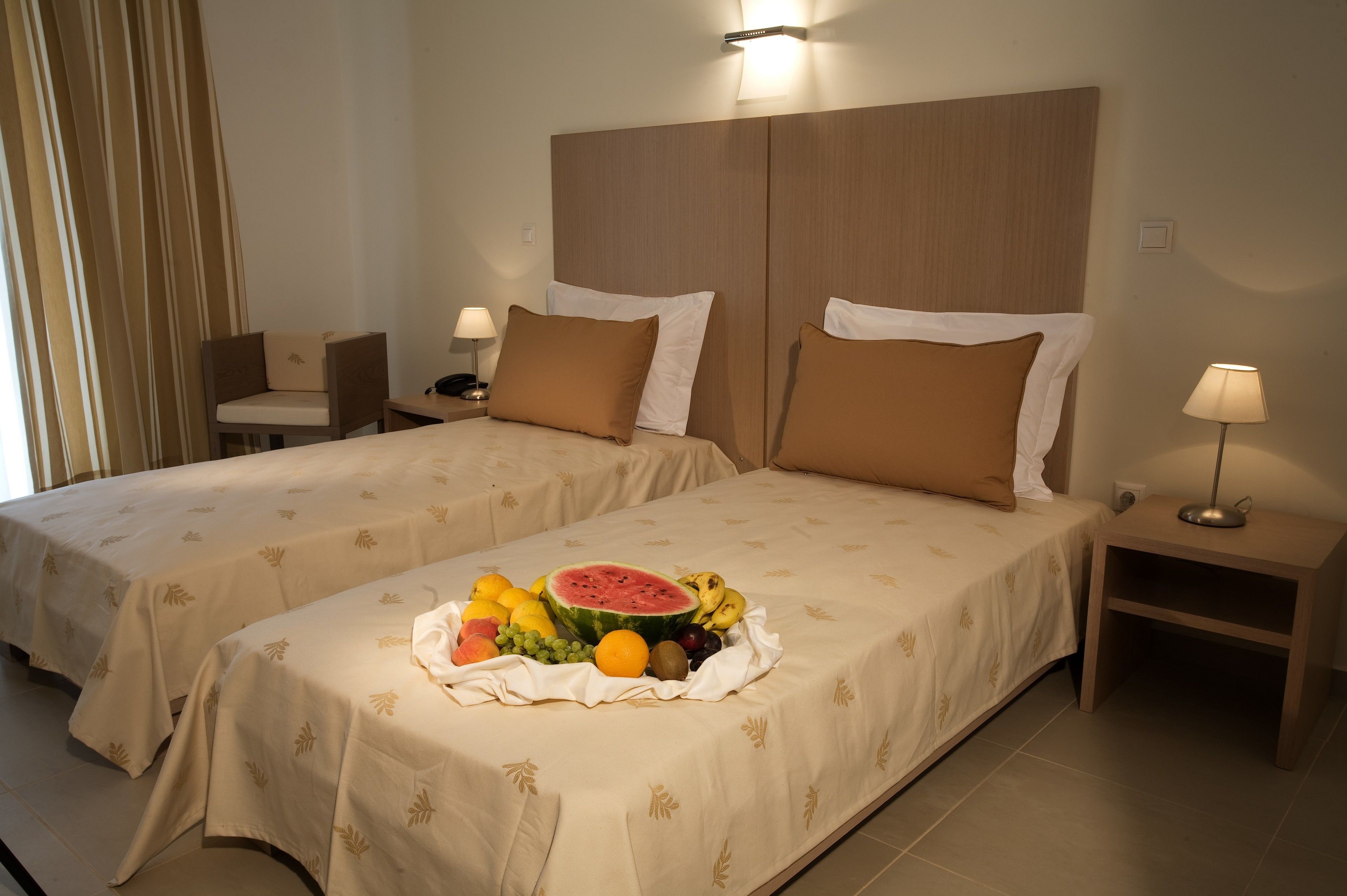 Quarto de hotel com duas camas, uma cesta de frutas sobre as camas e abajures.