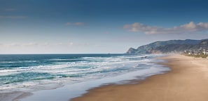 Uma praia com ondas, areal e uma montanha ao fundo.