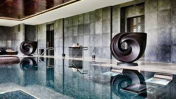 Piscina interior moderna com água cristalina, grandes esculturas abstratas e um painel de parede de pedra.