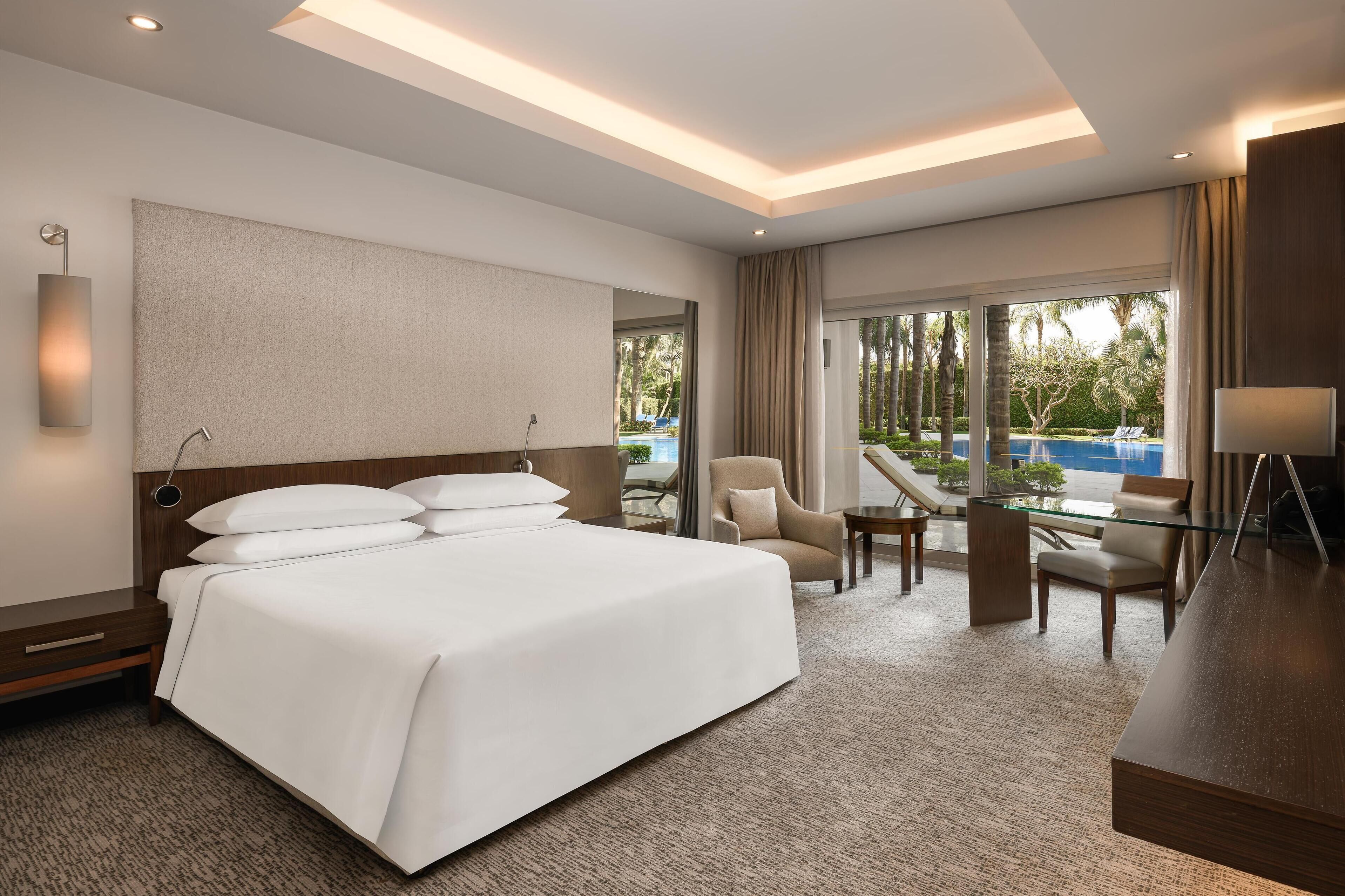 Quarto de hotel moderno com uma cama grande, uma escrivaninha e vista para uma piscina.