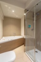 Uma casa de banho moderna com cabine de duche em vidro, banheira independente e sanita.