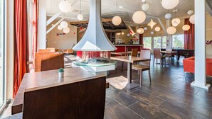 Interior moderno de restaurante com mesas de madeira, ilha central com bancada de vidro e luminárias pendentes esféricas.