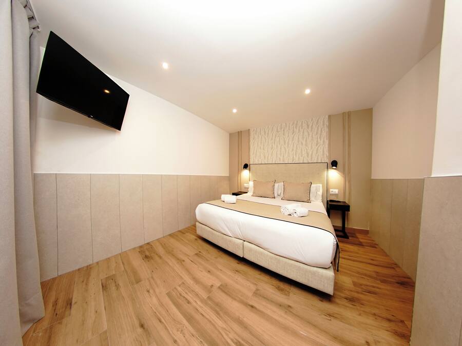 Quarto de hotel moderno com uma cama grande, uma TV de tela plana na parede e piso de madeira.