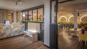 Um lobby de hotel moderno com uma recepção, área de estar e vista para o restaurante.