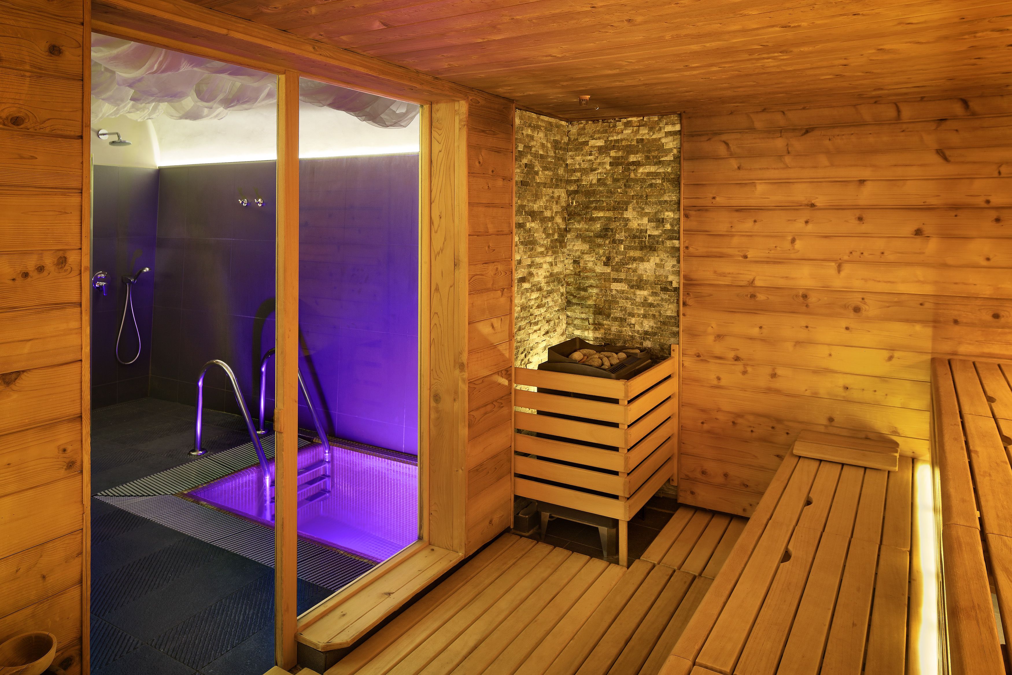 Uma sala de sauna de madeira com porta de vidro, banco de madeira e parede de pedra.