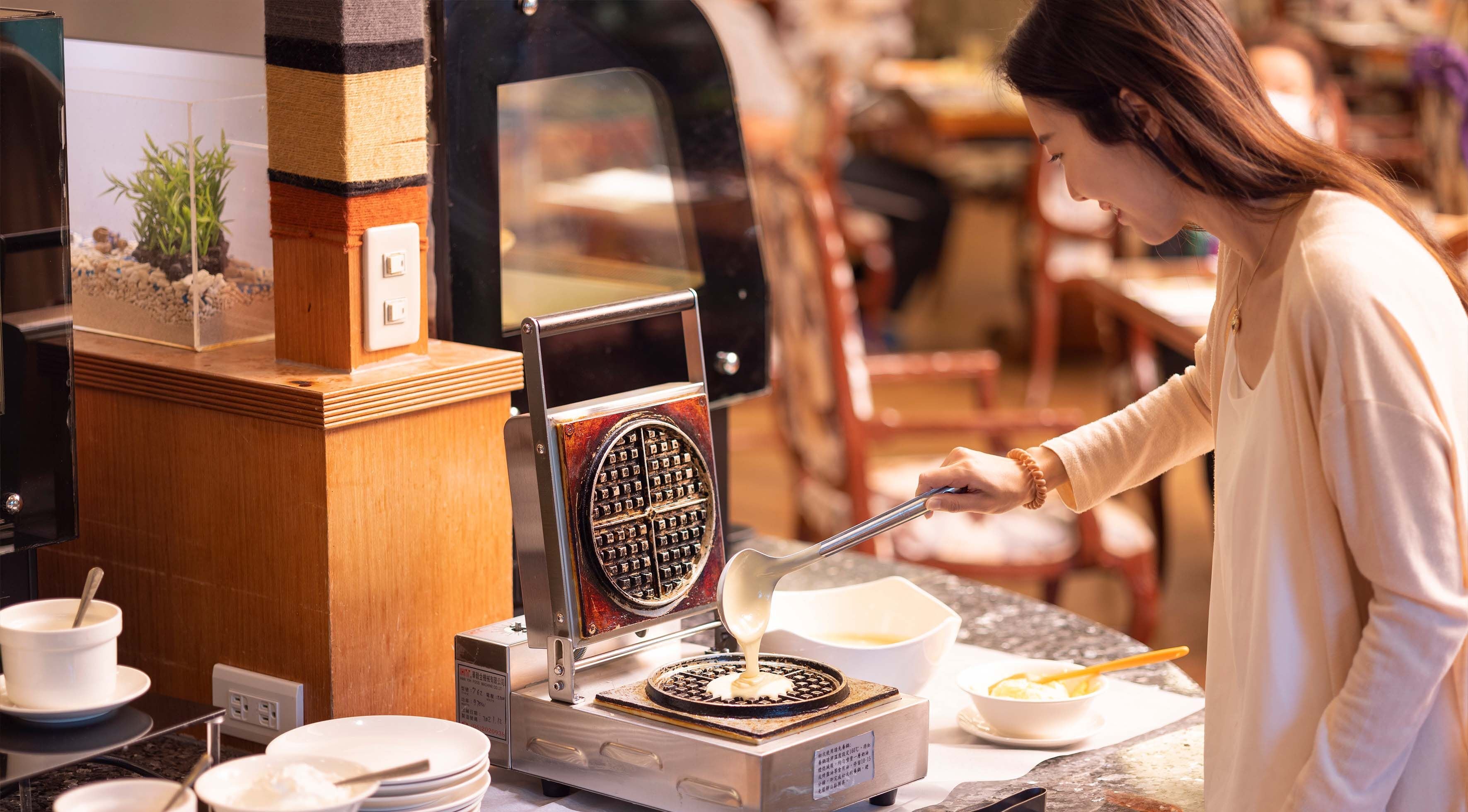 Máquina de waffles com alguém despejando massa dentro.