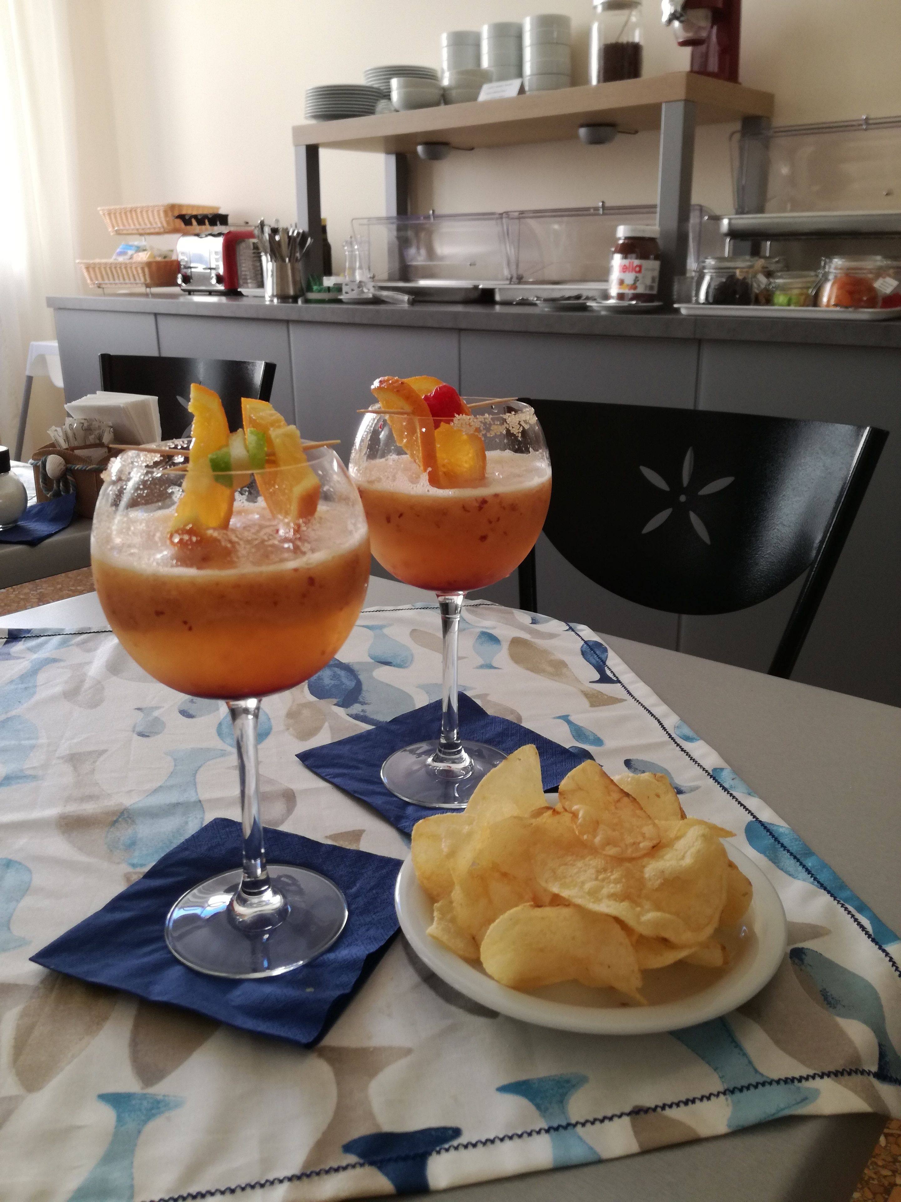 Duas bebidas com guarnições de frutas sobre uma mesa com um prato de batatas fritas.