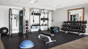 Academia com equipamentos de ginástica, um banco, uma bola medicinal e um suporte com halteres.