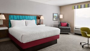 Quarto de hotel com uma cama grande, uma escrivaninha, uma cadeira e uma janela.