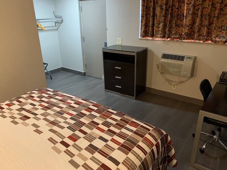 Quarto com cama, escrivaninha, cadeira, guarda-roupa e ar condicionado.